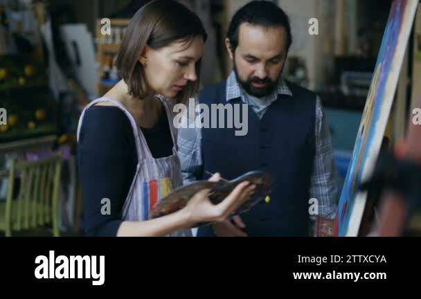Skilled artist man teaching young girl to draw paintings and explaining ...