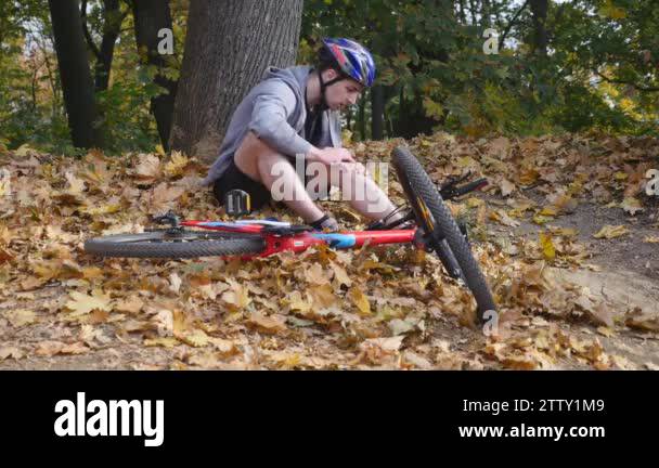 A young man sits in a park after falling from a bike, calms the pain in ...