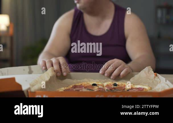 Obese man looking around and devouring fatty pizza at night, junk food ...