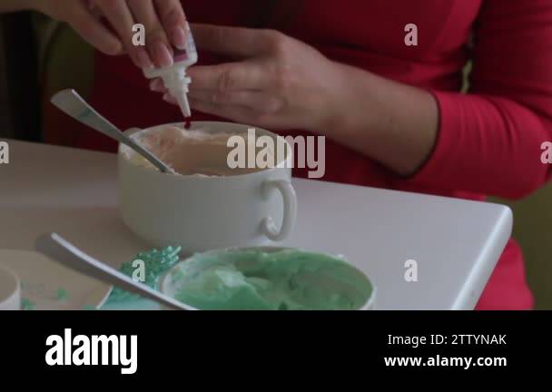 A woman adds a drop of food coloring from a tube of cream cheese ...