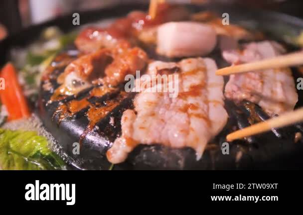 People using chopstick to cooking pick up and flip pork and meet of Korean BBQ barbecue on the ...