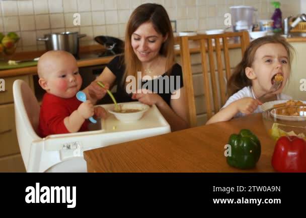Smart housewife feeds her two children in the kitchen. The kid is ...