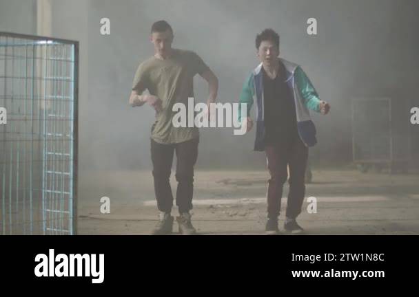 Two confident young men dancing in the dark and dusty room of abandoned ...