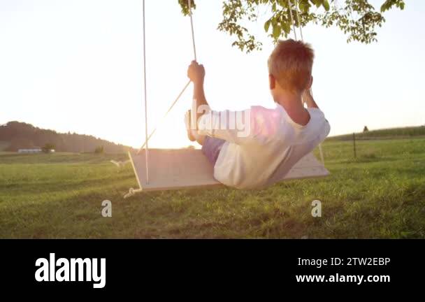 SLOW MOTION CLOSE UP: Unrecognizable child swinging on a wooden swing ...
