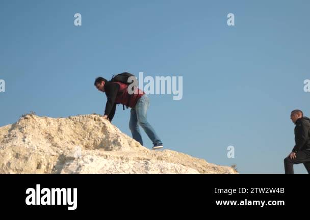 tourists give hand to each other, climbing to top of the hill. team of male travelers goes to ...