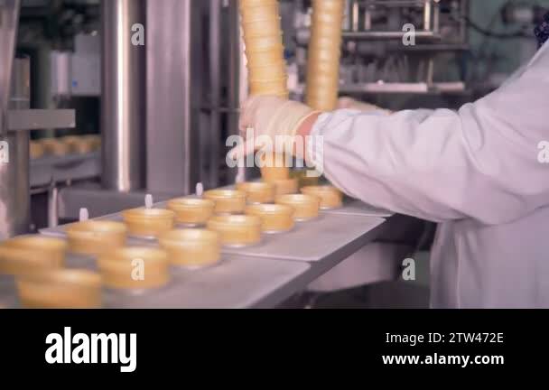 A factory worker is putting empty wafer cups into holes on the conveyor ...