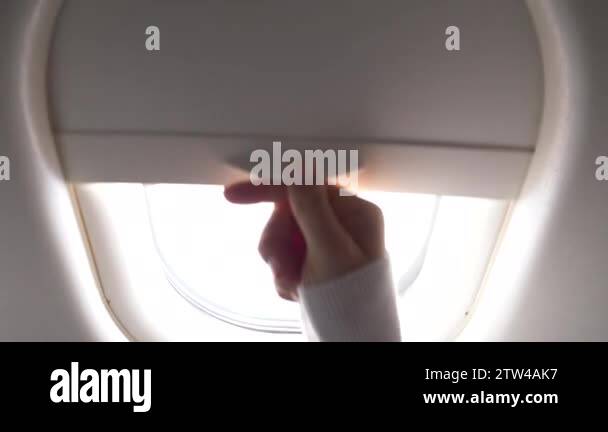 CLOSE UP: Woman traveler pulls up the blinds and looks through airplane ...