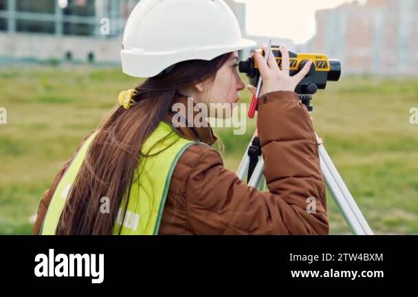 young woman surveyor in green work clothes and helmet adjusts the ...