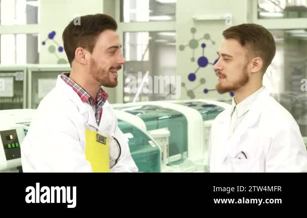 Two young lab technicians stand in the middle of the laboratory and ...