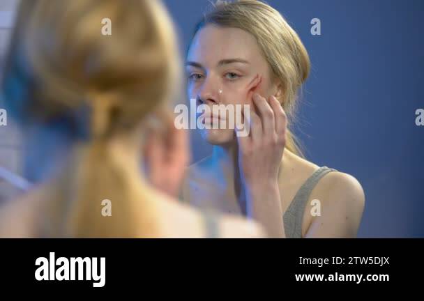 Sad female victim looking at face wound in mirror, domestic violence ...