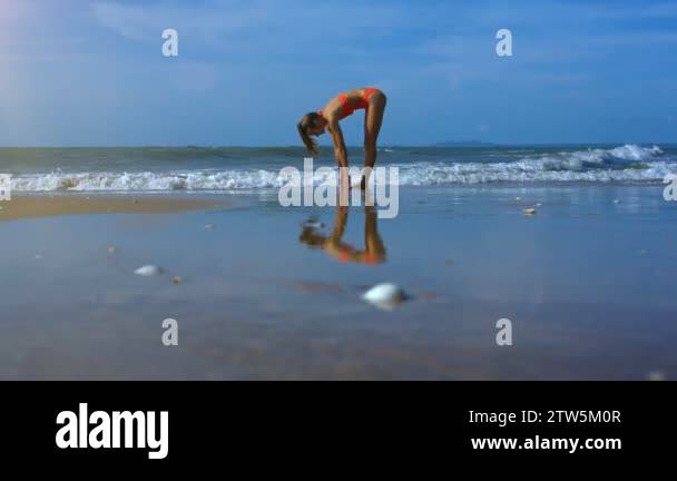 slim girl figure in swimsuit holding yoga pose reflects in shallow ...