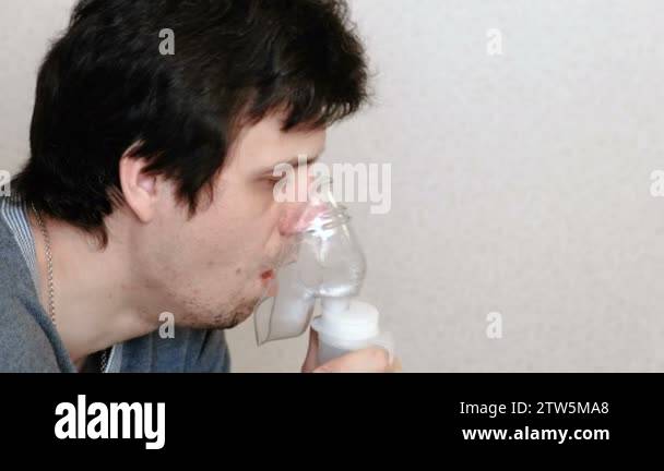 Use nebulizer and inhaler for the treatment. Young man inhaling through ...