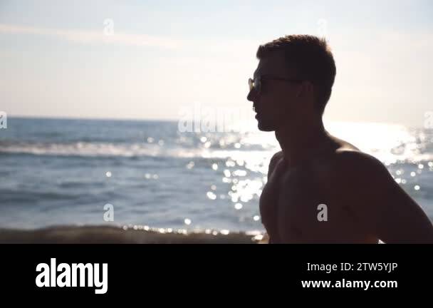 Profile of athletic guy in sunglasses jogging along sea coast. Young ...