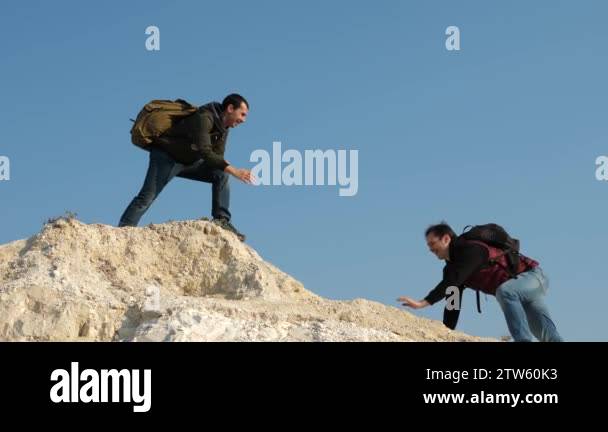 two climbers climb one after another on white rock. teamwork of business people. tourists give ...