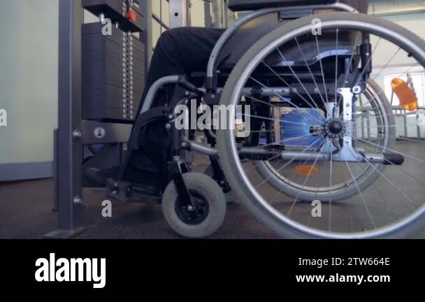 Side view of a disabled man lifting weights in a gym while sitting in a ...