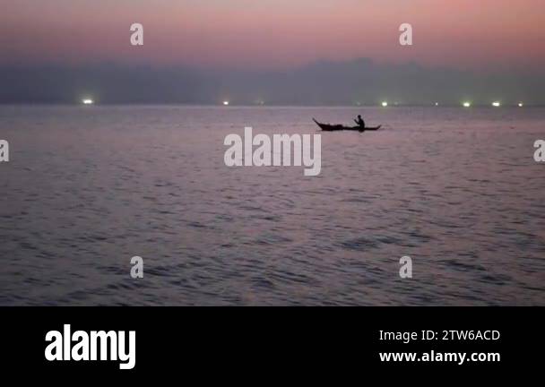 Person on shallop between lights of fishing ships in sea at sunset ...