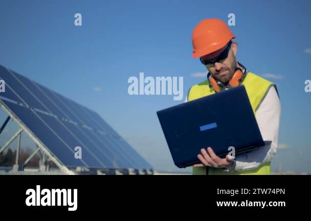Worker types on his laptop, standing next to sun panels on the building ...
