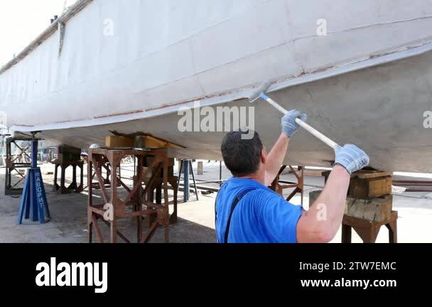 Worker paints metal of old rusty ship propeller at shipyard in port ...