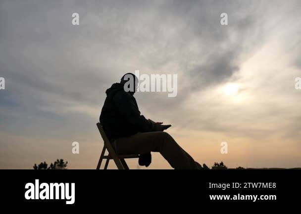 50 years old man silhouette turning pages of book outdoors approaching ...