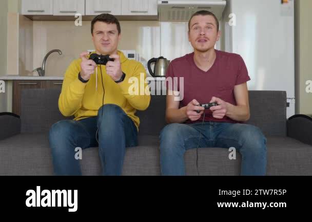 Two men are playing video games and lose. Young guys are sitting on the ...