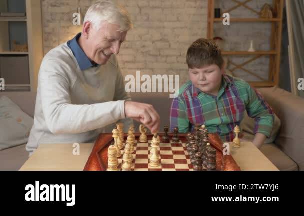 Grandfather and grandson plays chess. Elderly man teaches chess to play ...