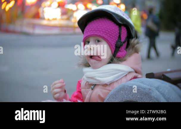 Beautiful little girl sitting on a bench in an amusement park, eating ...
