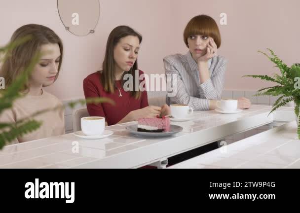 Three young Caucasian girls sitting in a cafe, drinking coffee, eating ...