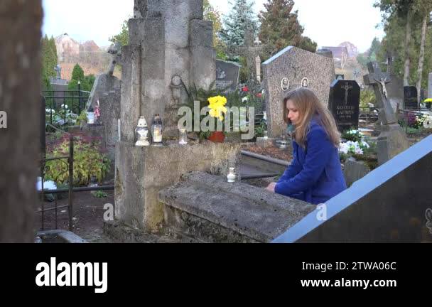Young sad woman girl on knees pray near old grave tomb in cemetery. 4K ...