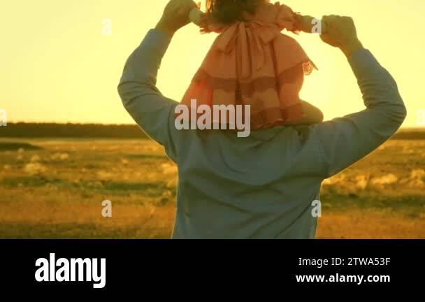 father walks with his daughter on his shoulders in rays of sunset. Dad carries on shoulders of ...