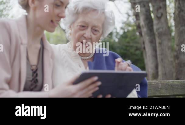 woman and senior grandmother using tablet device for video call at park ...