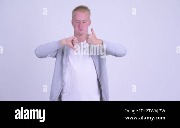 Confused young blonde man choosing between thumbs up and thumbs down ...