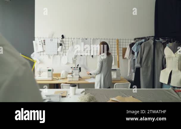 Back view of creative female tailor taking sketches from tailoring desk ...