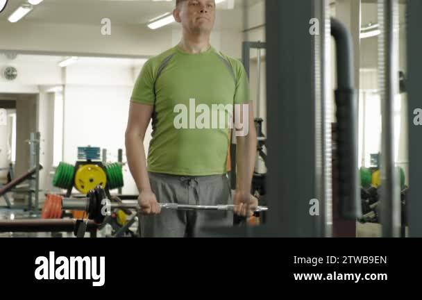 A overweight man lifts an ez barbell while standing at the gym ...