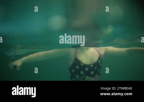 Smiling little girl without swim goggles swimming underwater in pool ...