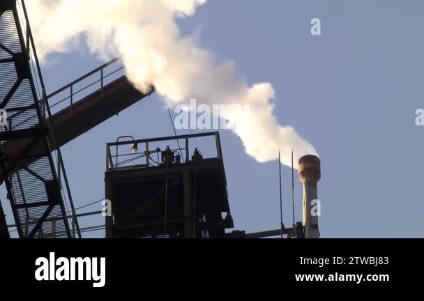 Old factory smoke stack billowing a white gray plume across blue and ...