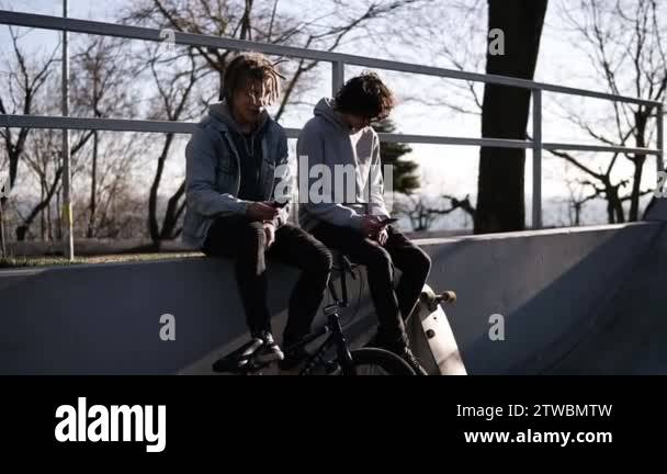 Two friends skateboarder and bmx rider are sitting together on high ...