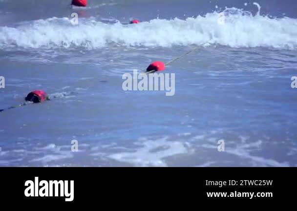 Red old enclosing buoys with green algae float on waves in the sea ...