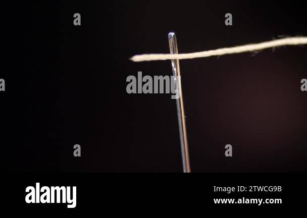 Threading the eye of a needle. Pulling the thread into the needle eye ...