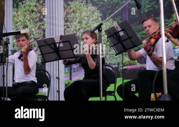 The ensemble of street musicians in open air. Women and men in black suits play classical music ...