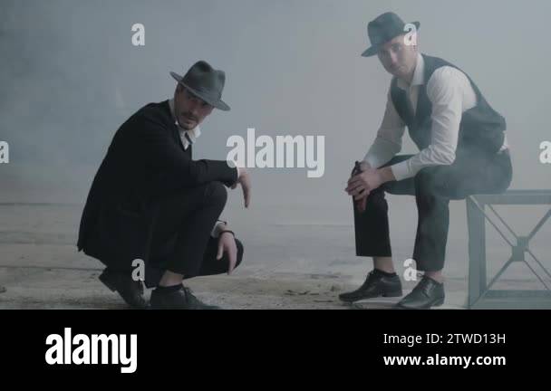 Two stylish men in hats, one sitting on the chair, another squatting in ...