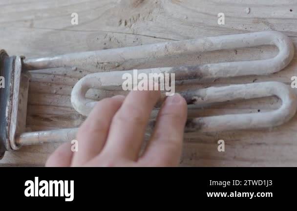 Burnt-out heating element from a washing machine. Man is touching ...