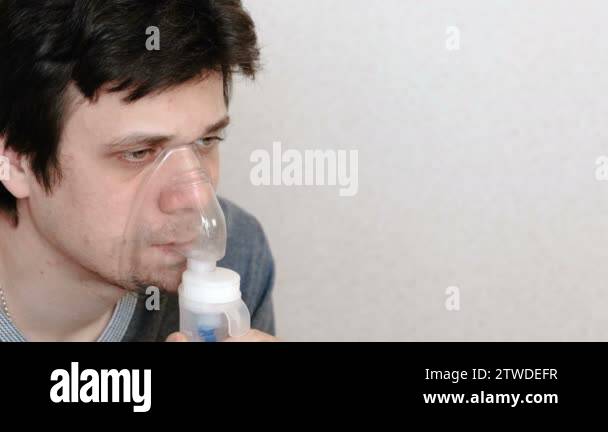 Use nebulizer and inhaler for the treatment. Young man inhaling through ...