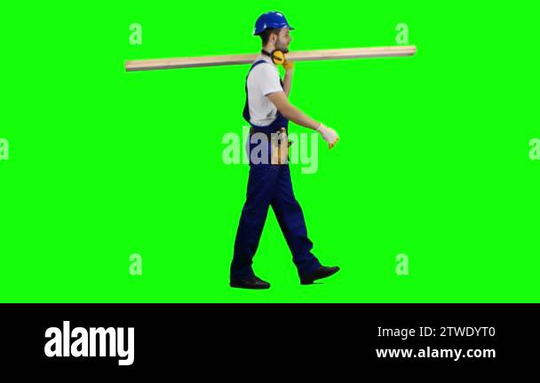 Builder in a helmet goes to work with wooden boards in his hands. Green ...
