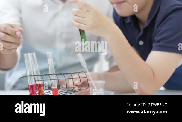 Teacher pouring chemical into test tube with his student in classroom ...