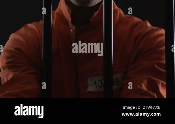 Policeman putting handcuffs on male prisoner standing behind cell bars ...
