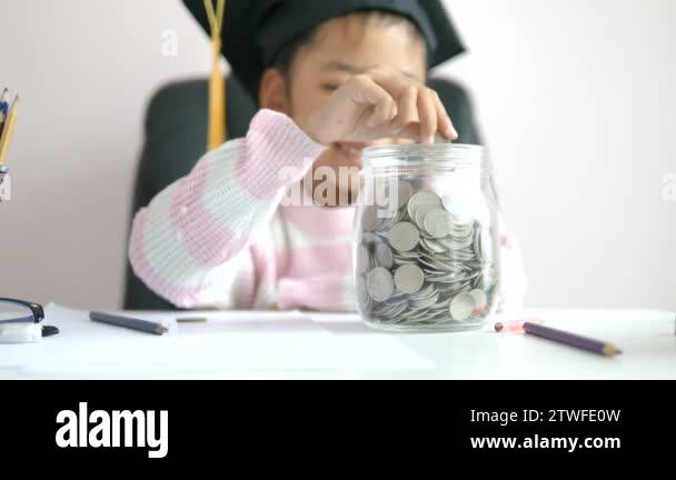 Little Asian girl puttinwg the coin into piggy bank and smile with ...