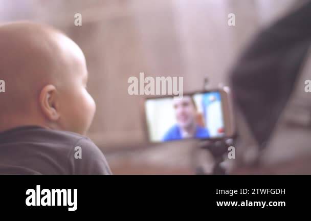 Baby boy looks at the Caucasian daddy on skype in a smartphone and ...