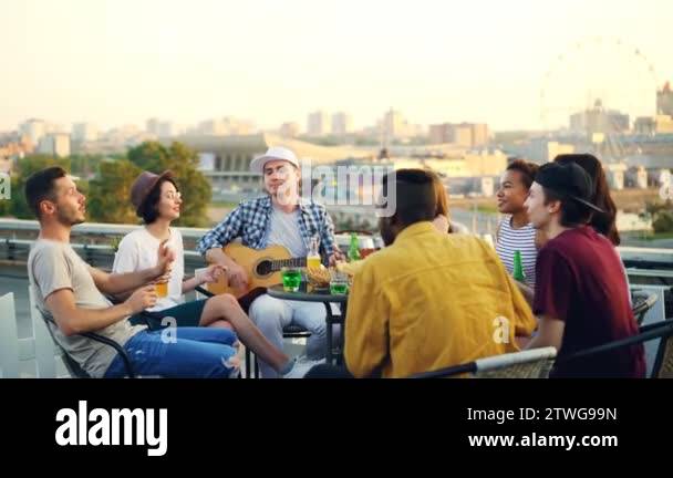 Students are having fun on rooftop playing the guitar, singing and ...