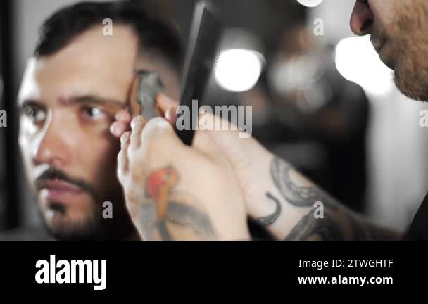 Tattoed barber makes haircut for customer at the barber shop by using ...
