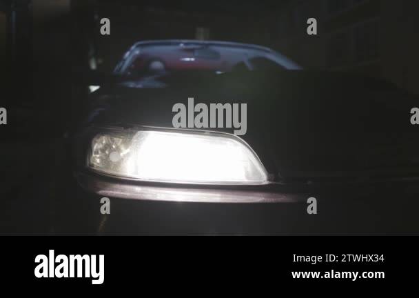 Close up for a headlight of a parked car being turned off at night ...